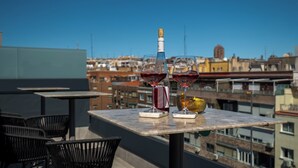 Terraço no telhado com uma mesa posta para dois, uma garrafa de vinho e duas taças de vinho tinto.
