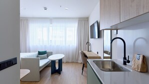 Cozinha moderna com pia, área de jantar com mesa e cadeiras, sofá e TV fixada na parede.
