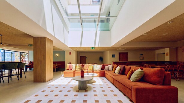 Um hall amplo com teto alto, área de estar central com um sofá vermelho, mesa de centro e piso estampado.