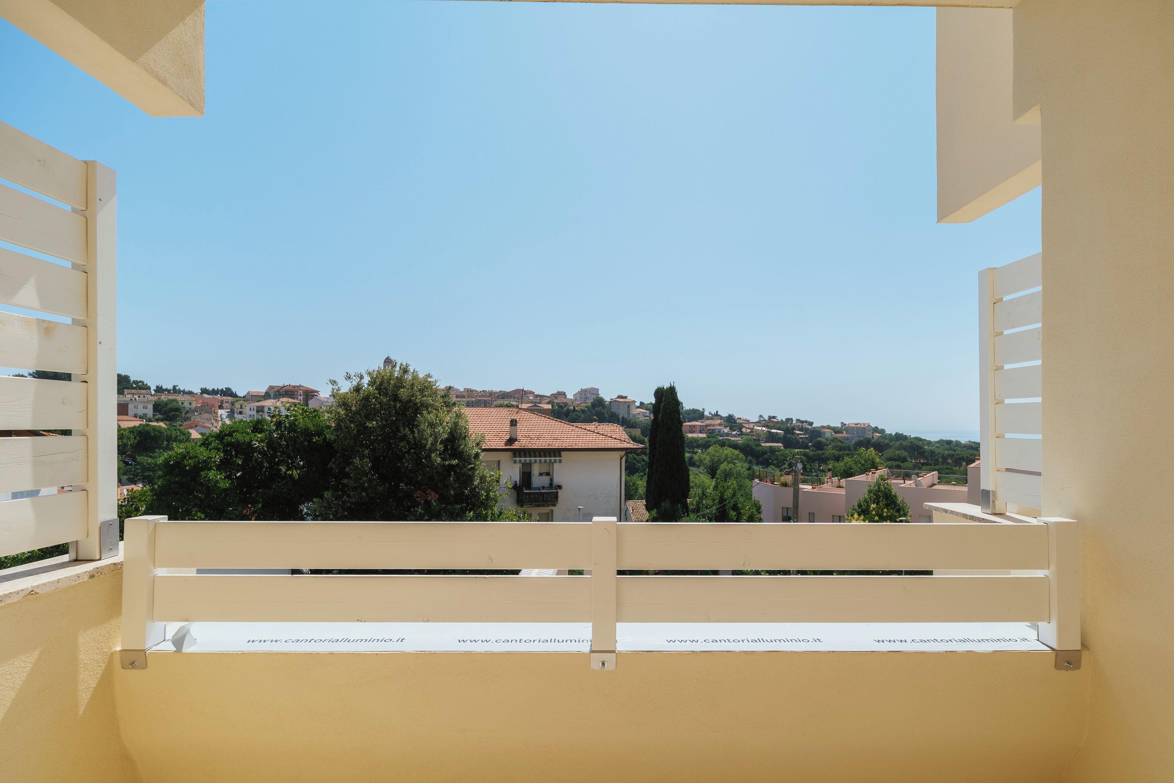 Varanda com grades brancas, vista para uma área residencial com casas e árvores.