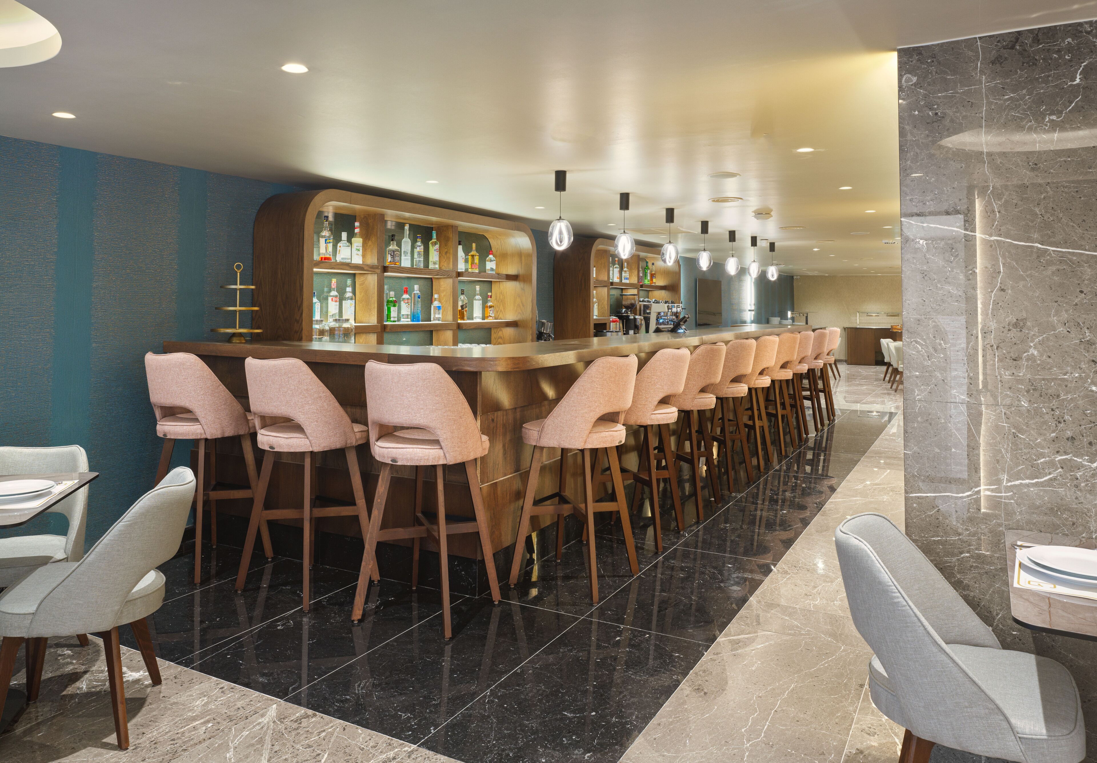 Uma área de bar com um balcão extenso, vários bancos altos e uma variedade de garrafas nas prateleiras.