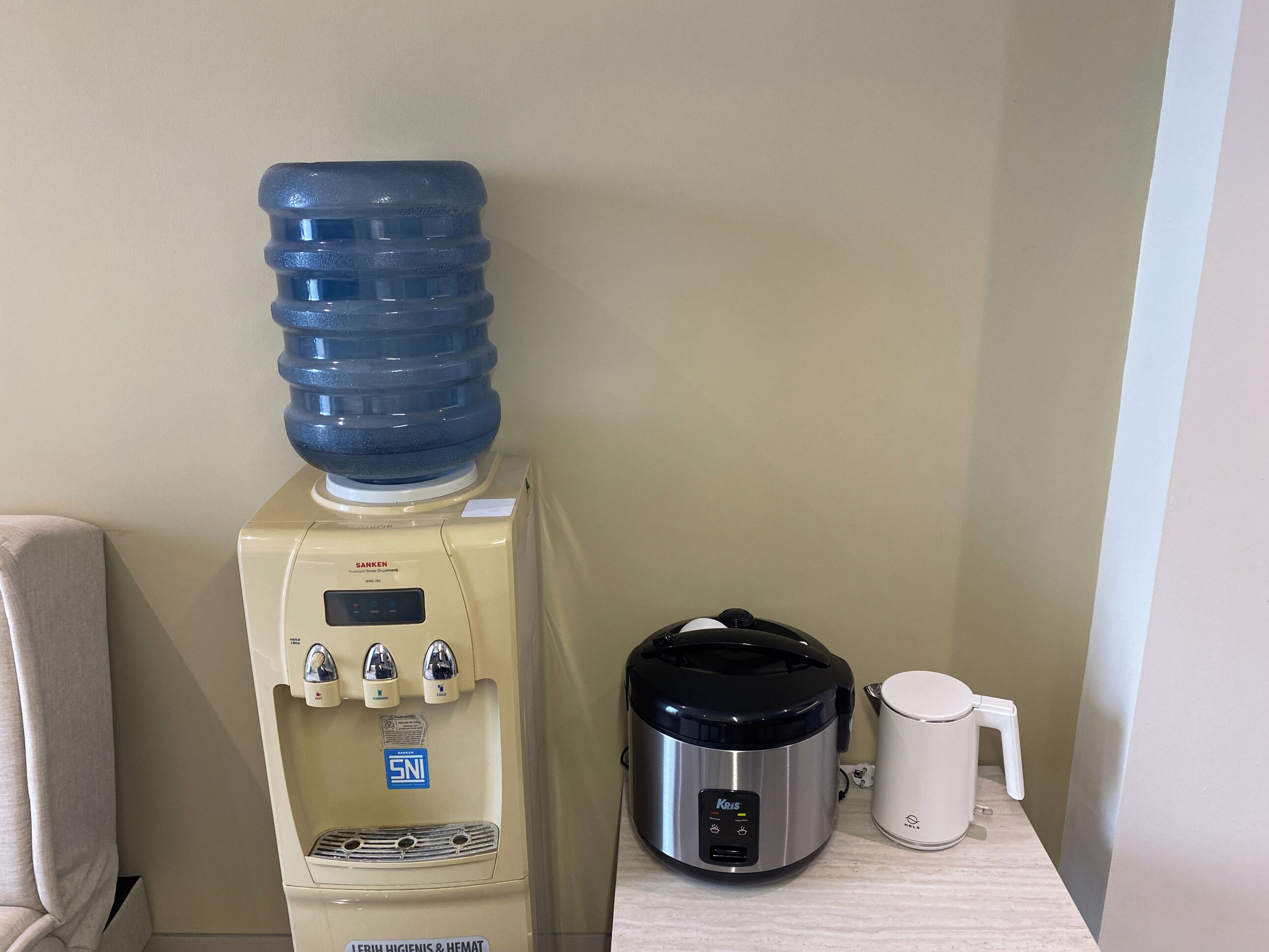 Um dispensador de água, uma panela de arroz e uma caneca branca sobre uma mesa.