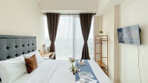 Quarto de hotel com uma cama grande, televisão fixada na parede e vista da cidade pela janela.