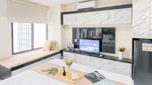 Quarto de hotel moderno com uma janela grande, televisão de tela plana na parede, ar condicionado embutido, uma pequena planta em vaso e uma bandeja com um vaso de flores.