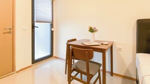 Um quarto pequeno e limpo, com uma mesa de madeira, uma cadeira, um vaso com flores e uma cama.