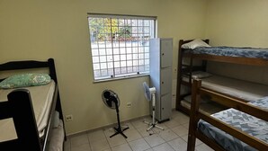 Um dormitório com beliches, uma janela com grades, um ventilador e um aquecedor.