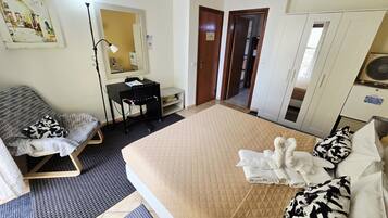 Quarto de hotel com uma cama, escrivaninha, cadeira, guarda-roupa e espelho.
