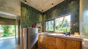 Uma cozinha moderna com azulejos verdes, armários de madeira, uma geladeira de aço inoxidável e uma janela com vista para o verde.