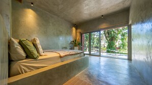 Quarto moderno com uma cama grande, uma mesinha e vista para o exterior por uma porta de vidro.