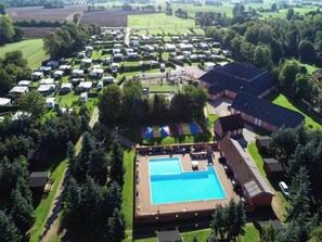 Vista aérea de um parque de campismo com veículos recreativos, piscina e um edifício grande.