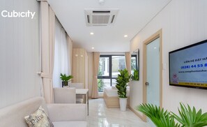 Um saguão de hotel com um sofá, uma mesa de centro e uma tela de televisão exibindo um número de contato.