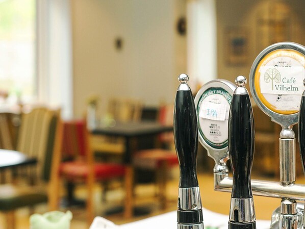 Uma fileira de torneiras de cerveja em um restaurante, incluindo uma torneira com a inscrição 'Café Vilhelm' e outra marcada como 'IPA'.