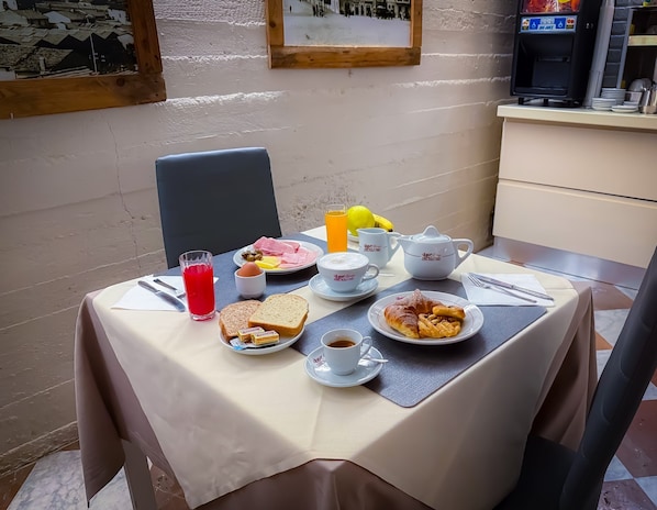 Mesa de pequeno-almoço com diversas opções de comida, um bule, chávenas e um dispensador de sumo.