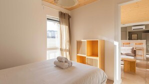 Quarto com cama grande, estantes de madeira, vista da cidade e cozinha compacta.