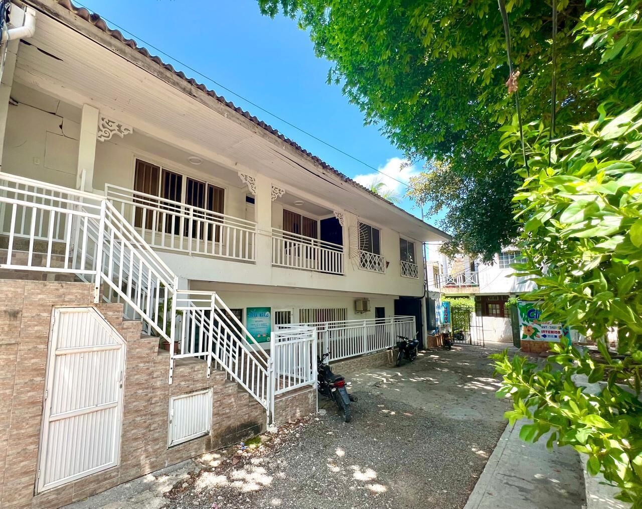 Um edifício de dois andares com varanda, escadaria e uma motocicleta estacionada na frente.