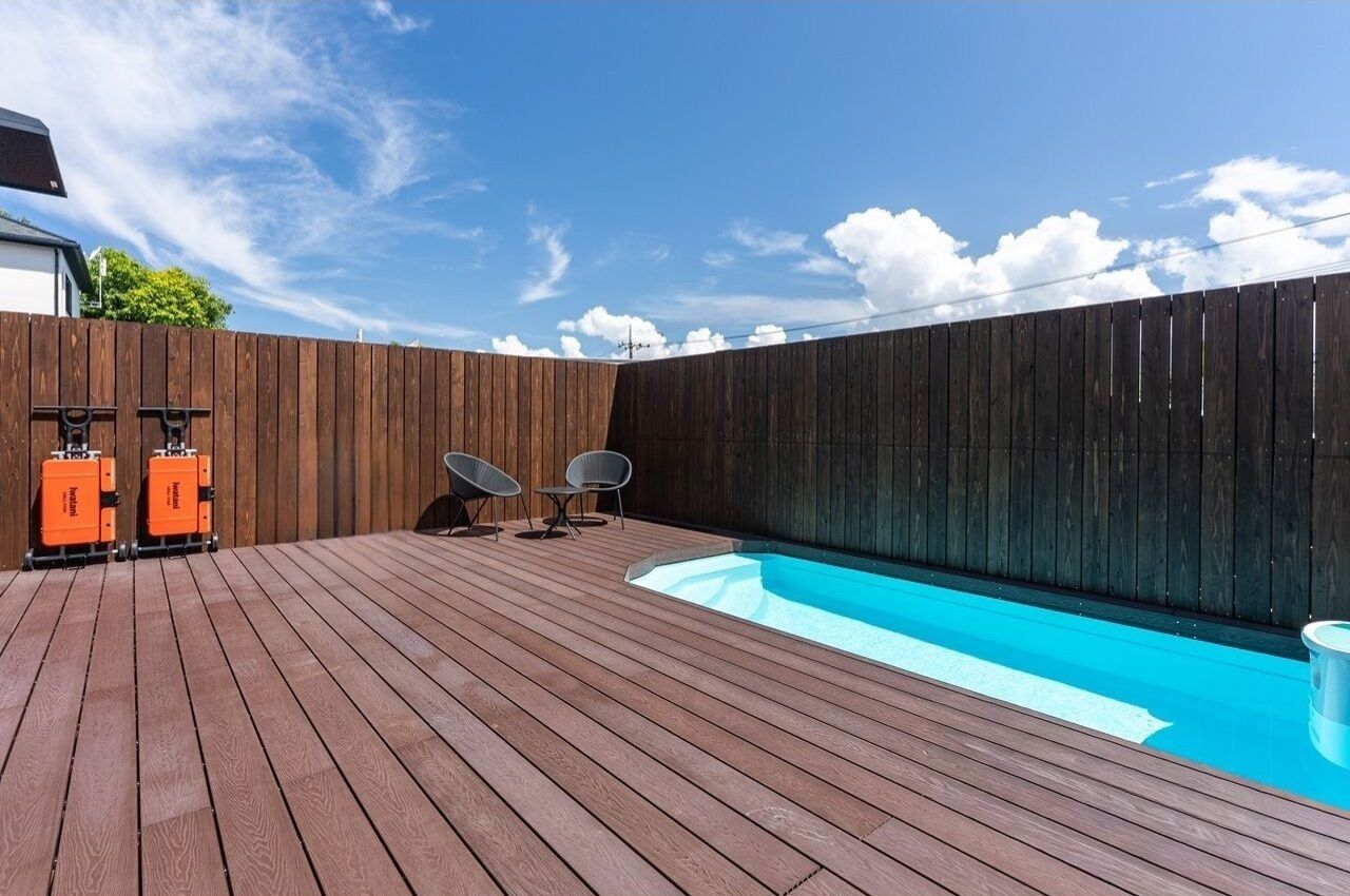 Um deck de madeira com piscina, duas espreguiçadeiras e dois alto-falantes laranja.