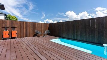 Um deck de madeira com piscina, duas espreguiçadeiras e dois alto-falantes laranja.