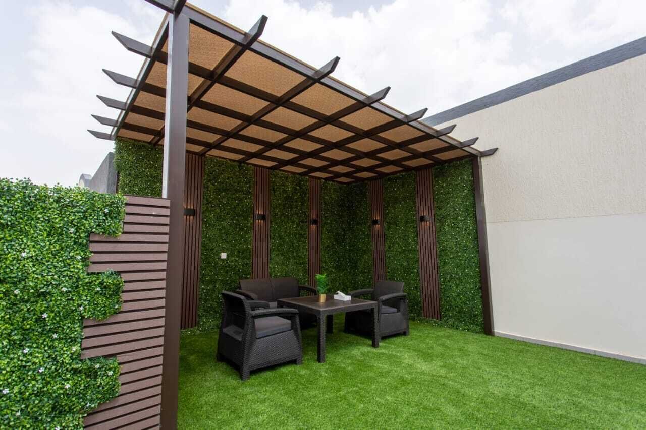 Área de pátio com pérgola, parede verde e mobiliário de exterior.