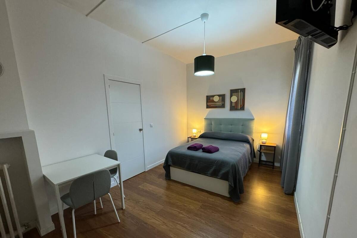 Quarto com cama, mesas de cabeceira, escrivaninha e cadeira.