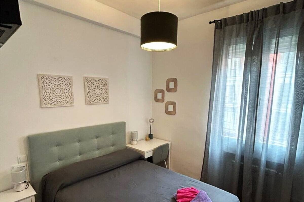 Quarto com cama, mesa de cabeceira, abajur e cortinas.