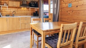 Interior de uma cabana de madeira com cozinha, mesa de jantar e cadeiras.