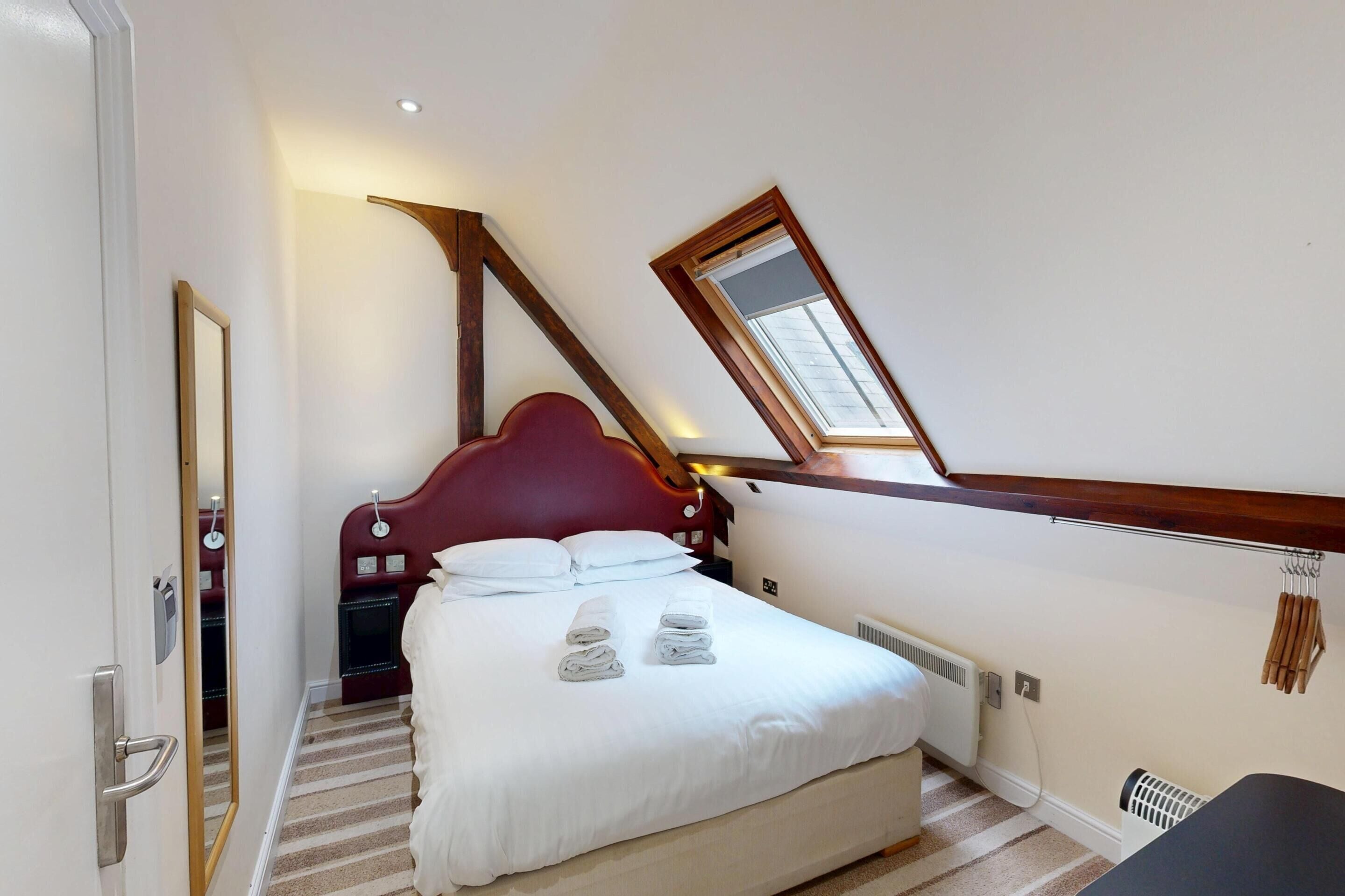 Quarto com cama grande, cabeceira vermelha, claraboia e vista do céu.