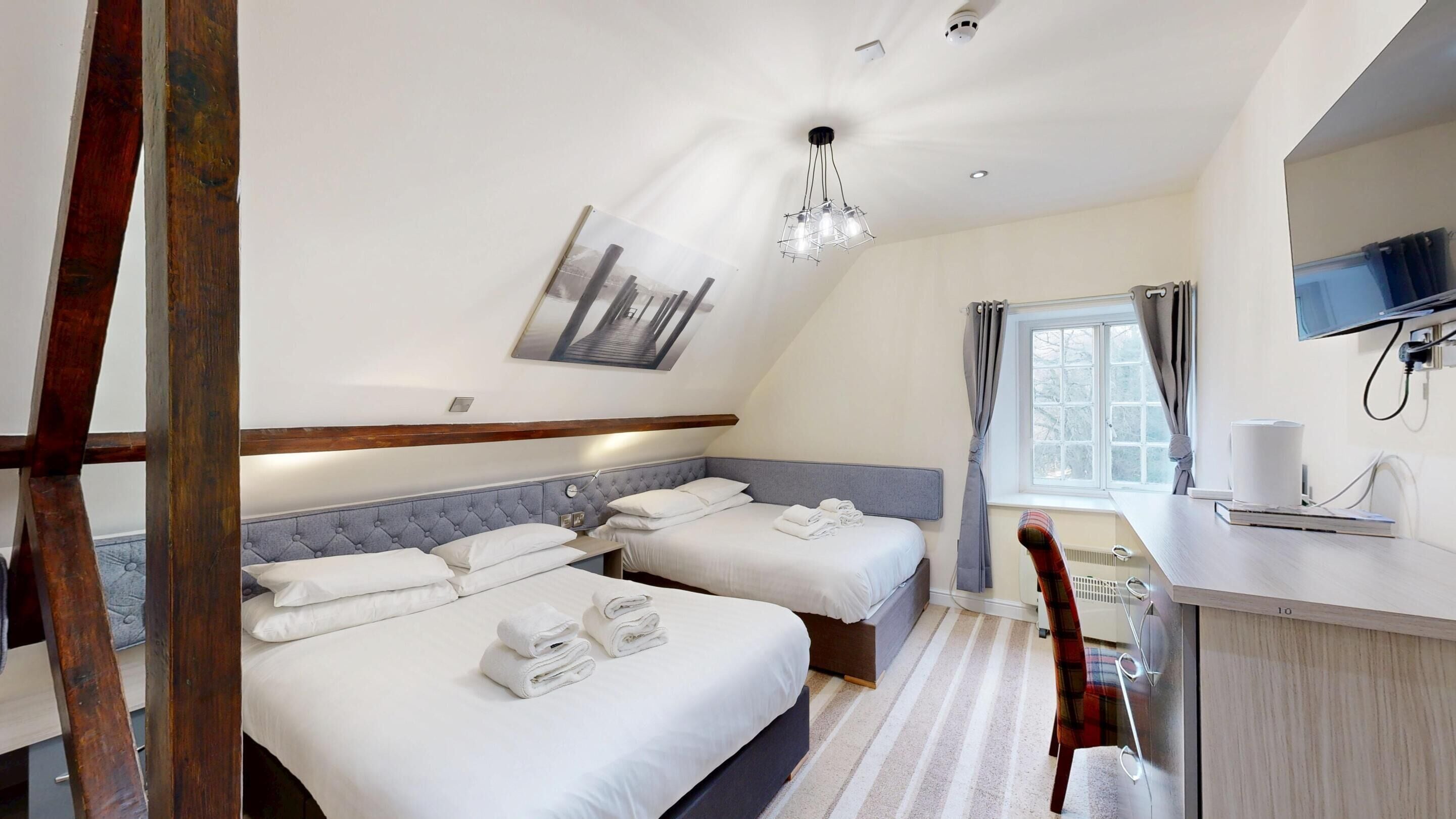 Quarto de hotel com duas camas, uma escrivaninha, uma cadeira, uma televisão e uma janela com cortinas.