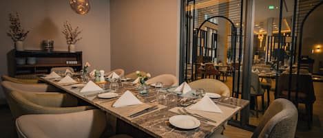 Uma sala de jantar com uma mesa comprida posta para refeição, rodeada por cadeiras estofadas.