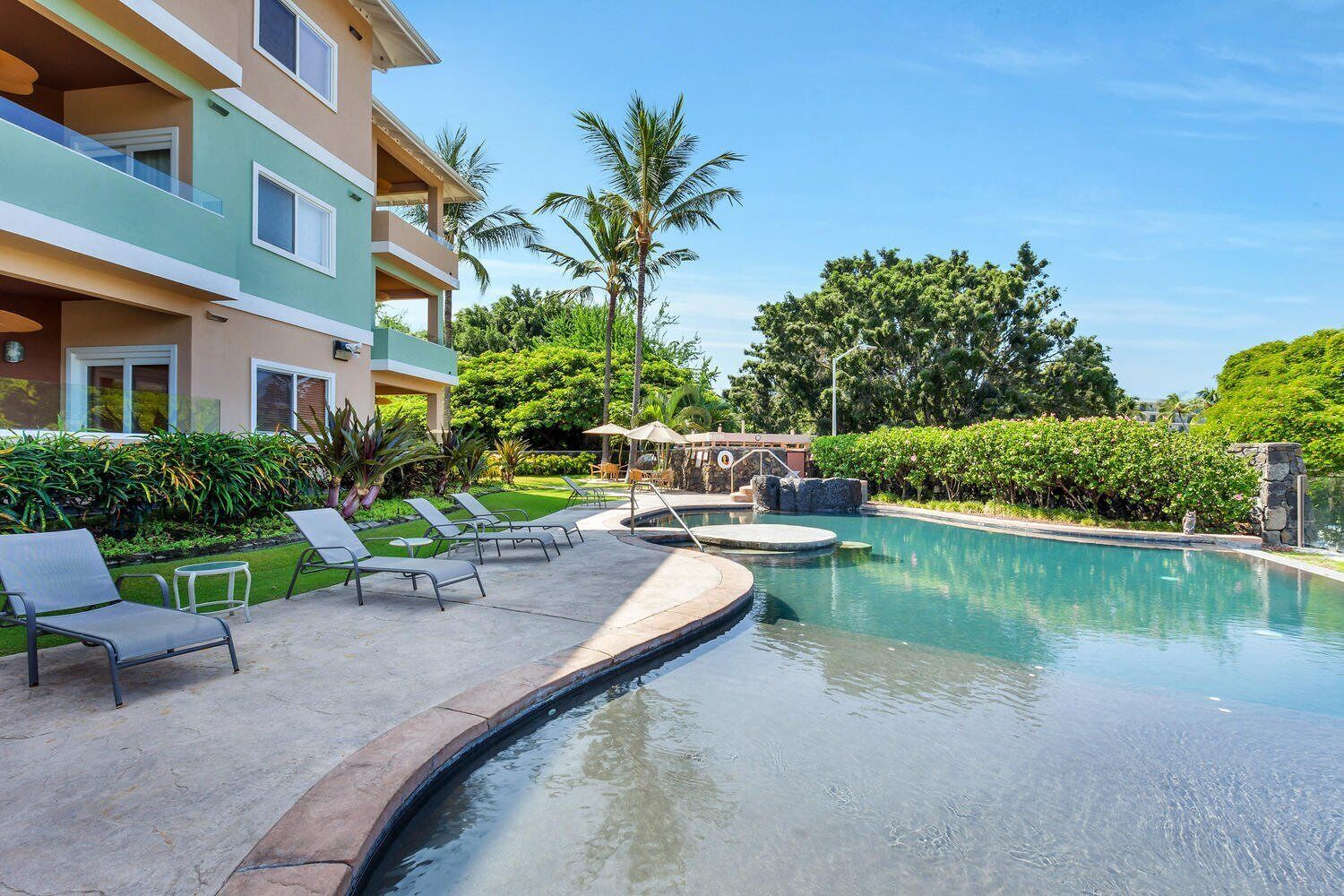 Uma área de piscina com espreguiçadeiras, uma piscina pequena e um edifício com varandas.