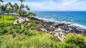 Paisagem costeira com um litoral rochoso, palmeiras e uma vista clara do oceano.