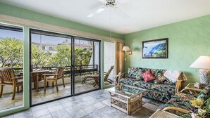 Quarto com porta de vidro deslizante que dá para área externa, sofá com padrão floral, mesa de centro de vime e ventilador de teto.