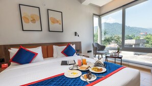 Quarto de hotel com uma cama grande, café da manhã servido na cama, uma cadeira e vista para as montanhas.