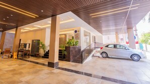 Um hall de hotel com design moderno, apresentando uma mesa de recepção, área de estar e uma escadaria para os andares superiores.
