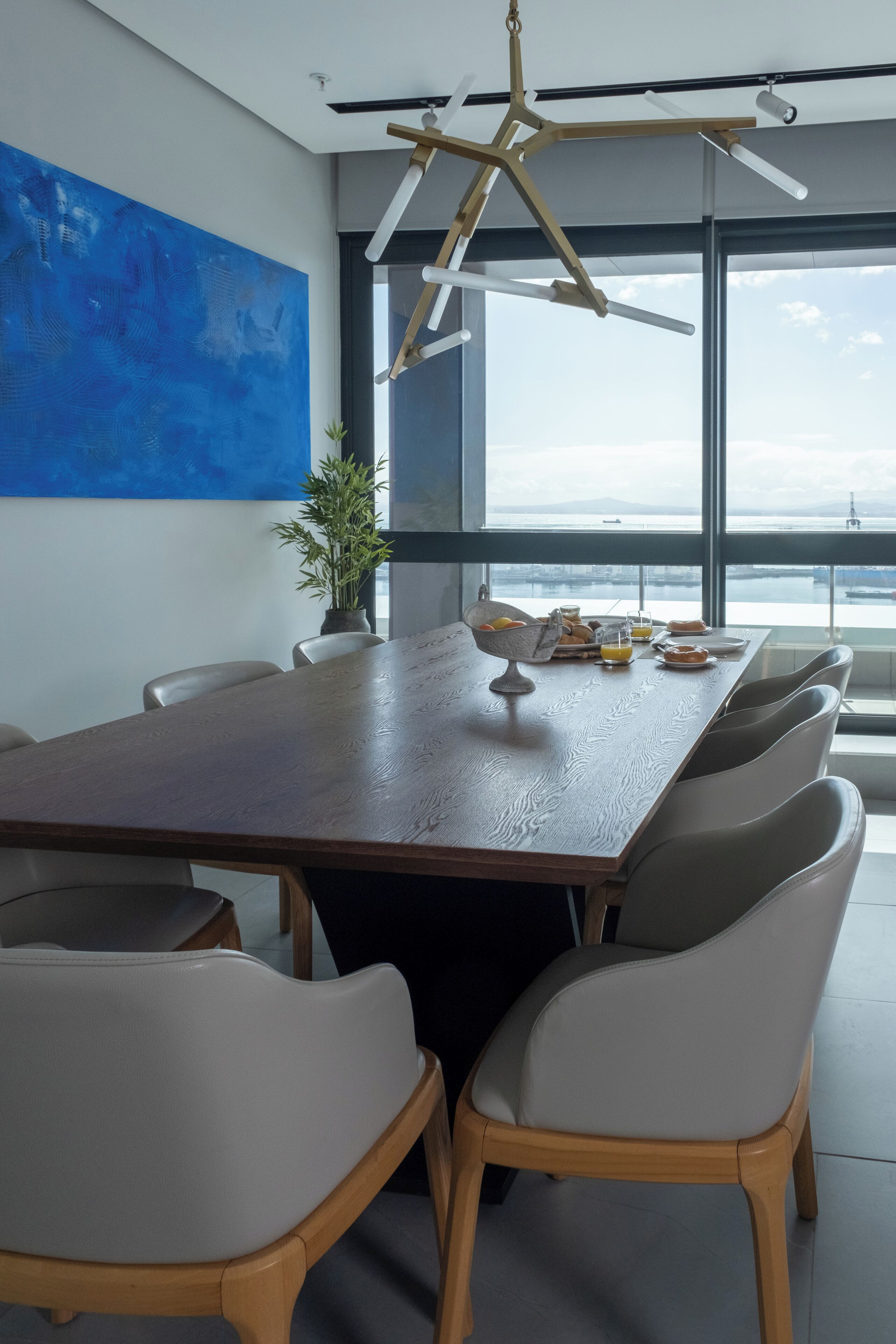 Uma sala de jantar moderna com uma grande mesa de madeira, cadeiras brancas e vista da cidade através de amplas janelas.