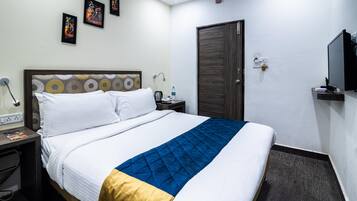 Quarto de hotel com cama, mesa de cabeceira, televisão e porta.