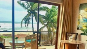 Quarto de hotel com uma cama grande, uma mesa pequena, uma cadeira e vista para o oceano e palmeiras.