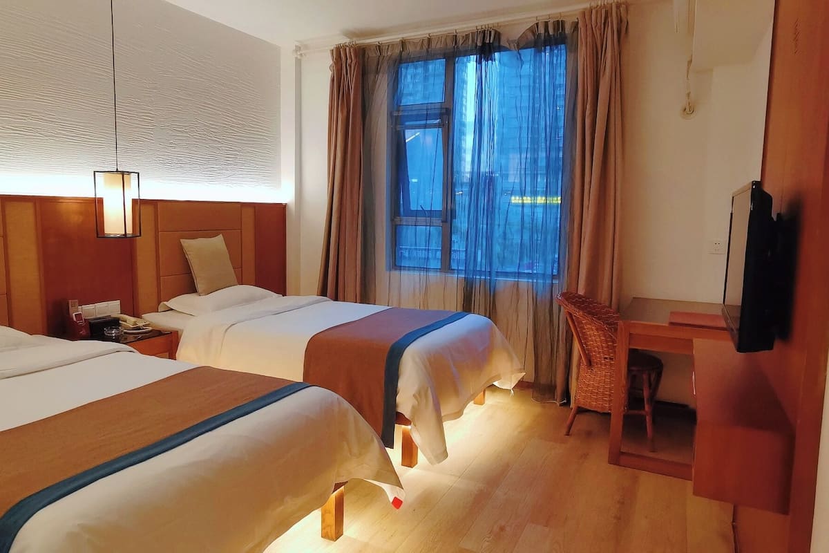 Quarto de hotel com duas camas, uma escrivaninha, uma cadeira e uma televisão.