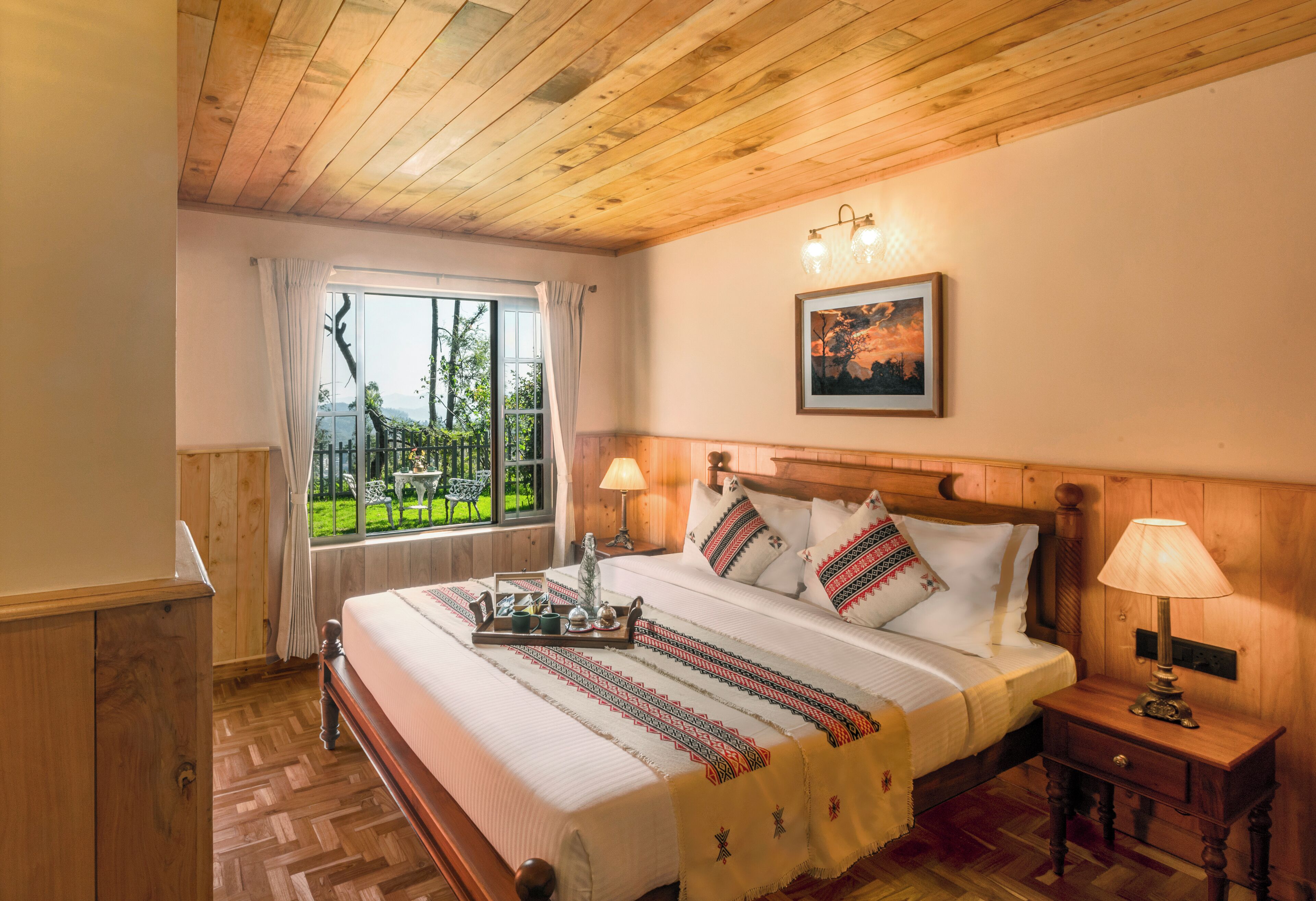 Quarto com painéis de madeira, uma cama grande, luminárias de cabeceira e uma janela com vista para o verde.