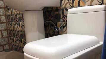 Um banheiro com vaso sanitário branco, azulejos estampados nas paredes e uma janela com vitrais.