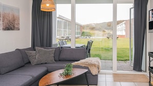 Uma sala de estar moderna com um sofá, uma mesa de centro e vista para o exterior através de grandes portas de vidro.