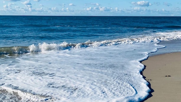 Uma praia com ondas suaves beijando a costa sob um céu claro.