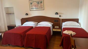 Quarto de hotel com duas camas, mesa de cabeceira com telefone, luminária na parede e um quadro.