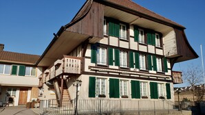 Um edifício tradicional com varanda, escadaria e um pequeno jardim.