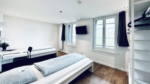 Um quarto moderno com uma cama, uma escrivaninha, uma cadeira, uma TV e uma janela.
