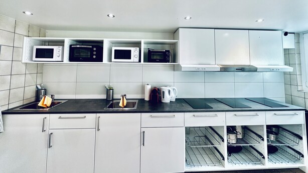 Uma cozinha moderna com armários brancos, bancada preta e três micro-ondas.