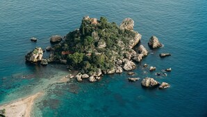 Vista aérea de uma pequena ilha com terreno rochoso e vegetação escassa, cercada por águas azul-claras.
