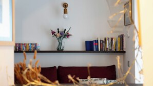 Um recanto aconchegante para leitura, com uma estante, um vaso de flores e um sofá confortável.