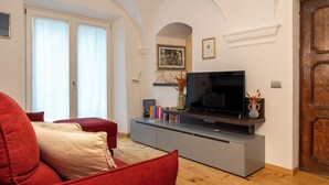 Uma sala de estar com uma televisão sobre um móvel cinzento, um sofá vermelho e uma porta de madeira.