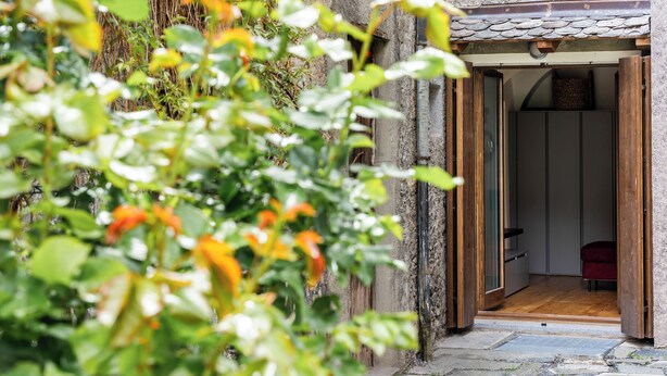 Uma entrada tradicional em estilo japonês, com porta de madeira e um pequeno banco de madeira no interior.