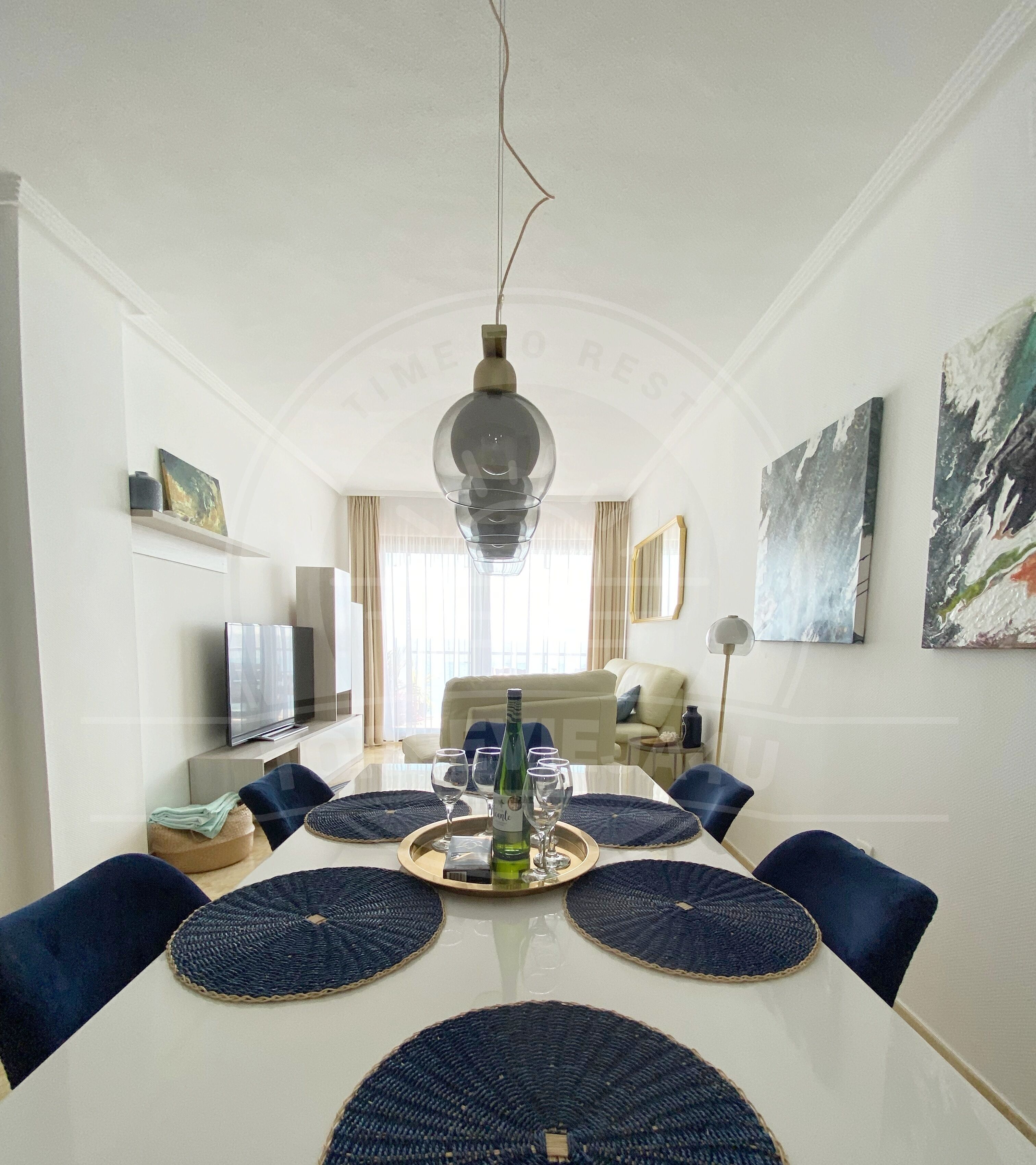 Uma sala de jantar com uma mesa branca, cadeiras azuis e um lustre.
